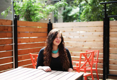 a woman sitting at a table in front of a wooden fence