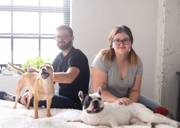 a couple sitting on a bed with two dogs
